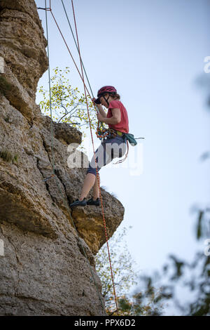 Photo of athlete girl clambering over rock against background of green ...