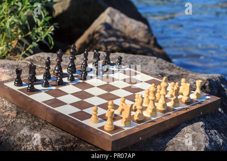 Chess board with chess pieces on a rock with the river embankment ...