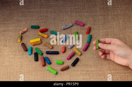 Hand holding a crayon by crayons forming a heart shape Stock Photo - Alamy