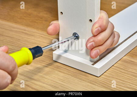 Furniture assembler tightens the cam lock nut with a screwdriver in the ...