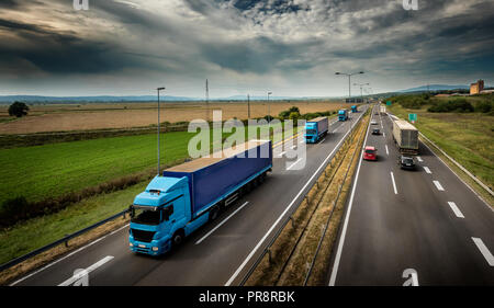 Convoy of blue lorry trucks on a country highway under amazing orange ...
