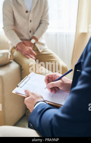 Close-up of a psychologist taking notes on clipboard while her patient ...