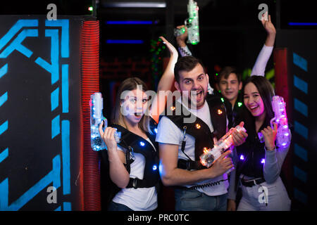 Group of young friends with laser guns playing laser tag game together ...