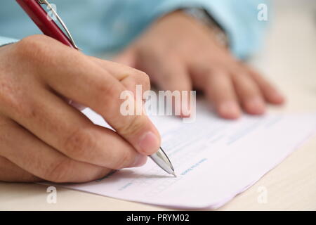 Man is filling form with pen. Picture of flower pot, computer, keyboard ...