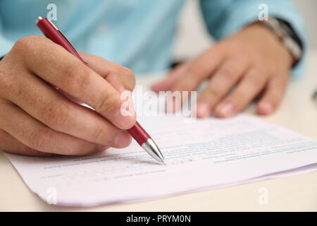 Man is filling form with pen. Picture of flower pot, computer, keyboard ...