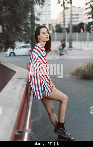 Portrait of woman wearing striped T-shirt holding laptop and pointing ...