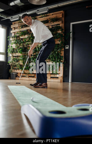 Businessman playing golf in office Stock Photo - Alamy