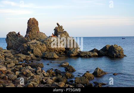 People on a basalt rock at the Cyclops islands, Aci Trezza, comune of ...