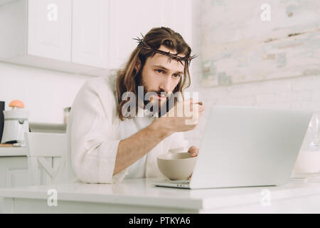 concentrated Jesus eating corn flakes on breakfast at table with laptop ...