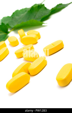 yellow vitamin pills over green leaf on white background Stock Photo ...