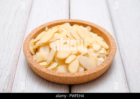 Sliced almond nuts in a wooden bowl and wooden spoon with cutting board ...