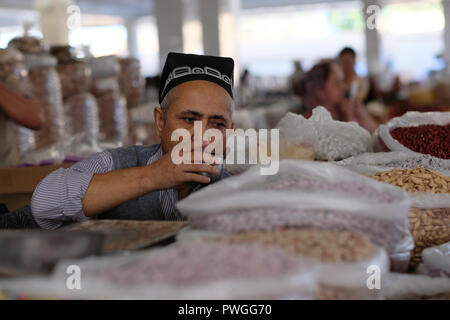 A vendor wearing traditional Uzbek doppa or duppi cap selling dried ...