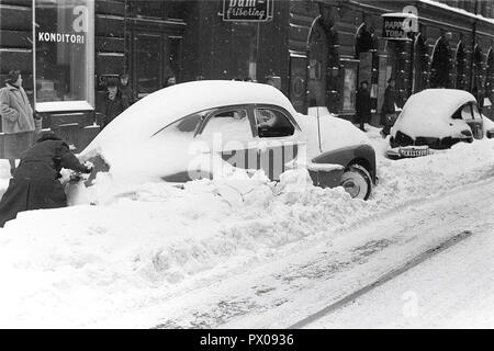 Winter driving in the 1950s. Snow has fallen heavily and the car parked ...