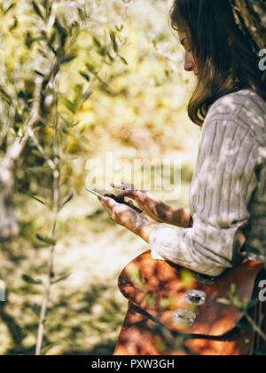 Italy, woman leaning against olive tree using cell phone Stock Photo ...