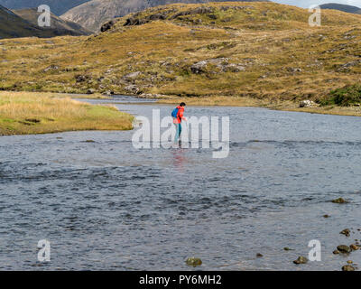 Lone female walker returning from Loch Coruisk crossing / fording river ...