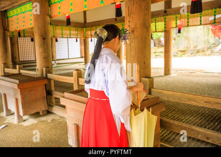 A shrine maiden in red and white robes in a courtyard at the ...