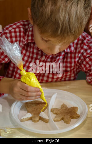 Boy in a plaid shirt is decorating with yellow cream the cookies in the ...