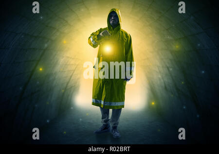 Ugly man in raincoat walking with glowing lantern in a dark tunnel ...