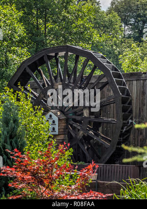 Wooden waterwheel in beautiful garden framed by two thin trees in South ...