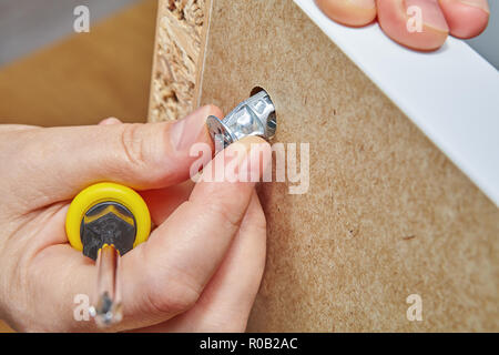 The furniture assembler fixes the cam lock nut in the leg of the wooden ...