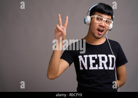 Young Asian nerd man listening to music against gray background Stock ...