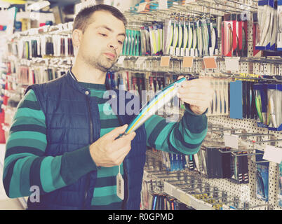 male customer selecting fishing lures near stand in the sports shop ...