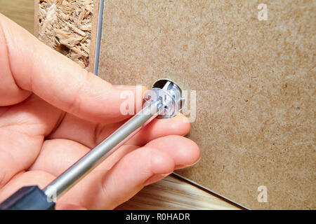 Furniture assembler tightens the cam lock nut with a screwdriver in the ...
