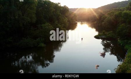 Aerial view of fisherman wading into calm Zumbro River at sunset, with ...