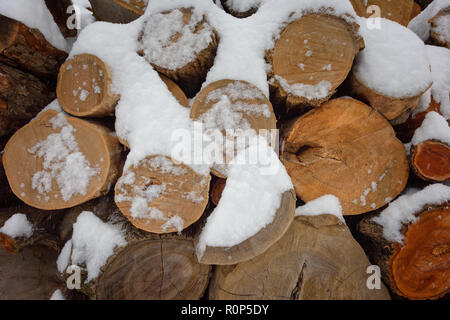 Faces of logs in winter. Woodpile of firewood under snow. Abstract ...
