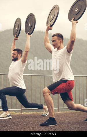 two athletes with barbell disc making lunges in outdoor workout Stock ...