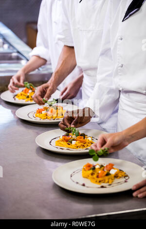 Male chef garnishing food with herb under light at commercial kitchen ...