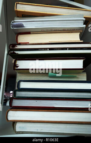 photograph of the sides of a pile of hardbacked books on a white shelf ...