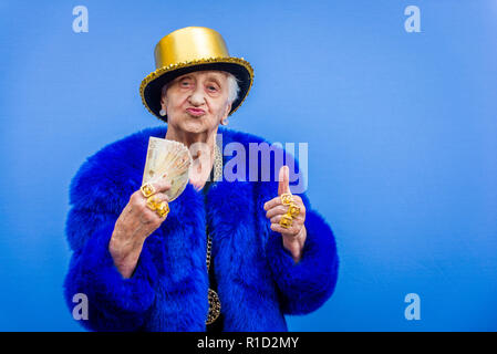 Funny and extravagant senior woman posing on colored background ...