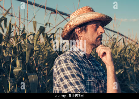 Serious thoughtful farmer in corn field, looking confident and ...