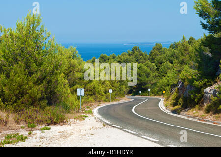 Empty road winding among rocks and lush green hills with pine trees ...