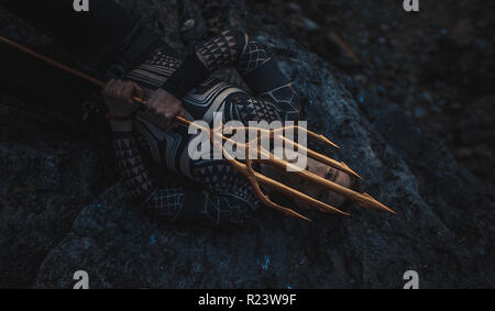 A young man in armor and with a trident in his hands lies on the rock ...