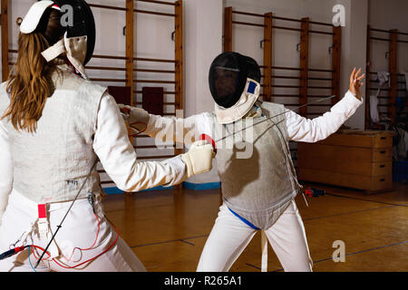 Two women fencers practicing techniques in duel at the fencing sparring ...