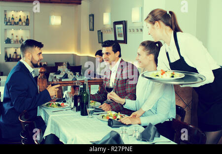 Attractive waitress serving meals to friendly company at restaurant ...