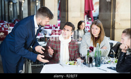 Displeased angry customers in restaurant sitting at table talking with ...