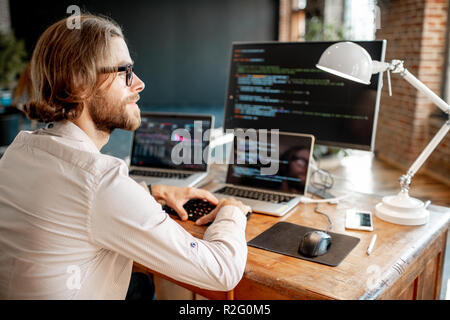 Young male programmer writing a program code sitting at the workplace ...