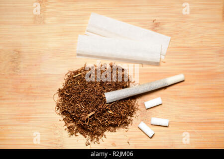 Hand rolling tobacco, paper and filters to make cigarettes on rustic ...