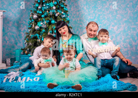 A large family are gathered around a christmas tree, adding decorations ...