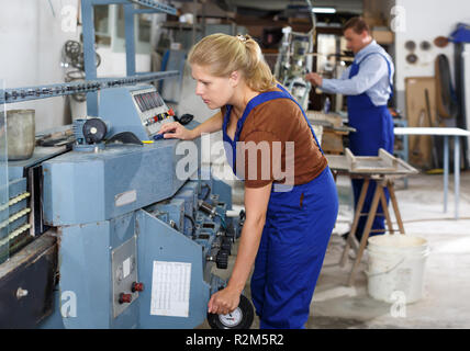 Confident female glazier working on glass straight line bevelling ...