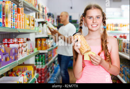 Positive tween girl choosing food products on shopping list in ...