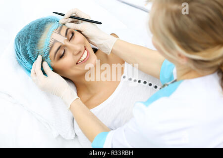 Professional beautician is going to correct eyebrow line at woman face ...