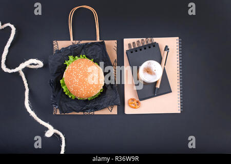 Big hamburger, beer and notebook for planning on a black background ...