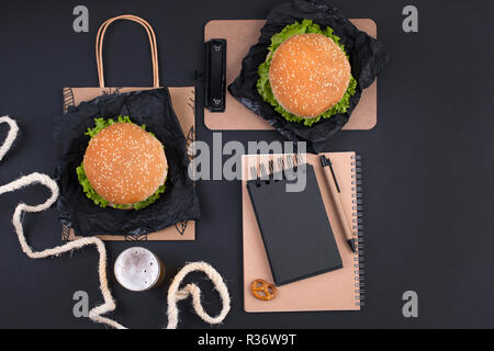 Big hamburger, beer and notebook for planning on a black background ...