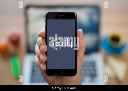 A man looks at his iPhone which displays the Zulily logo (Editorial use ...