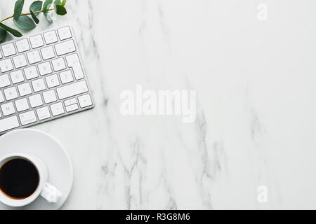Computer keyboard with cup of coffee and eucalyptus branch on pink ...