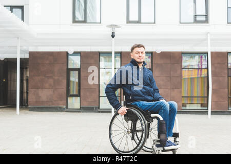 Young man in a wheelchair against the backdrop of a modern high-rise ...